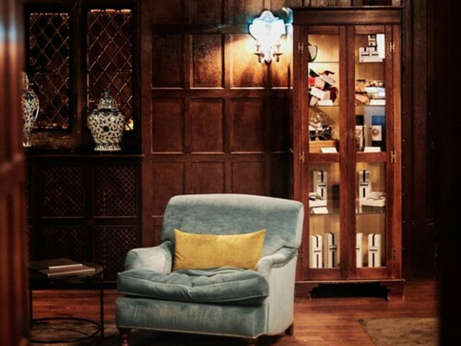 Um quarto com uma poltrona azul, um armário de madeira com portas de vidro e papel de parede estampado.