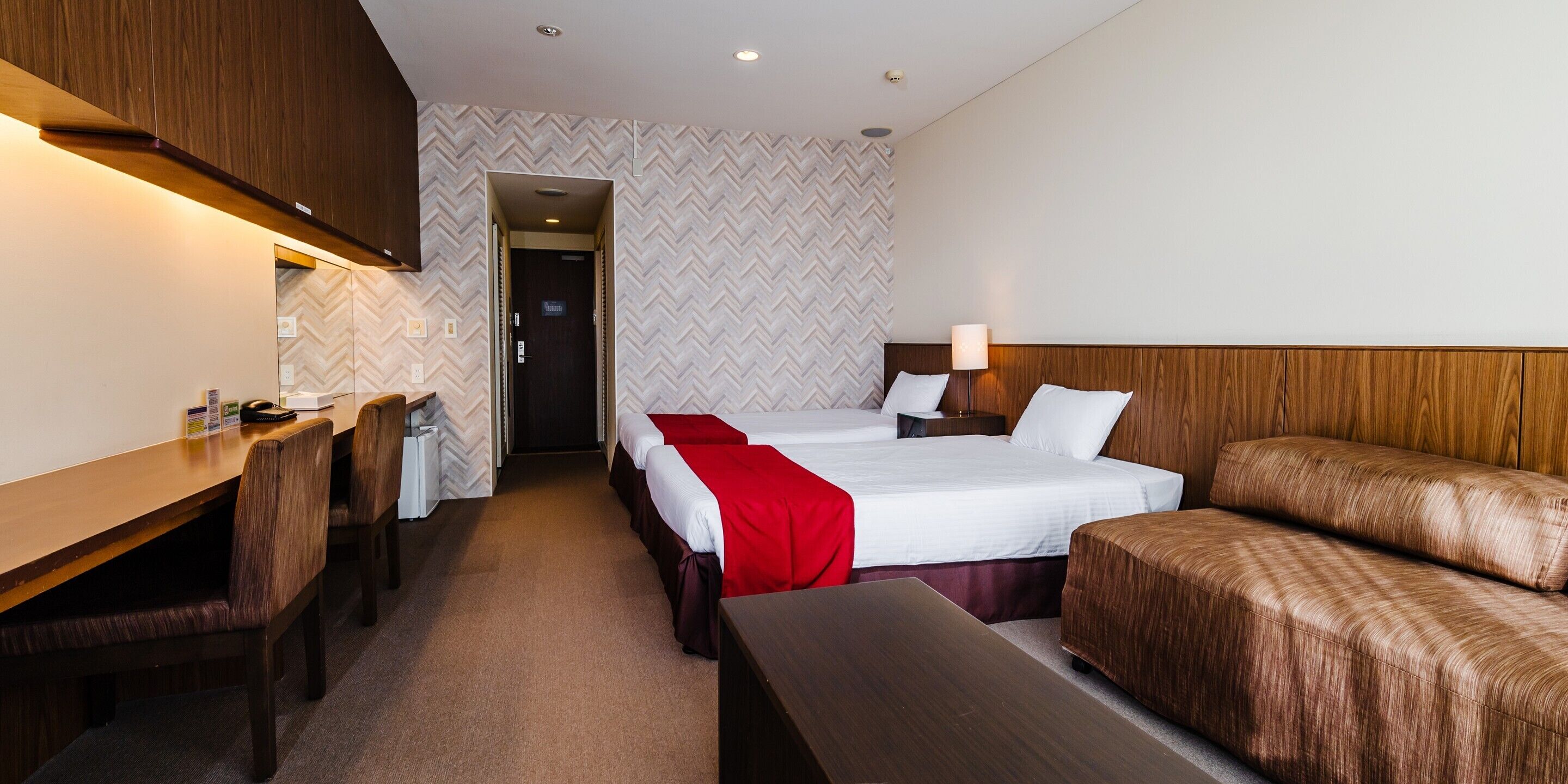 Quarto de hotel com duas camas, uma escrivaninha e uma cadeira.