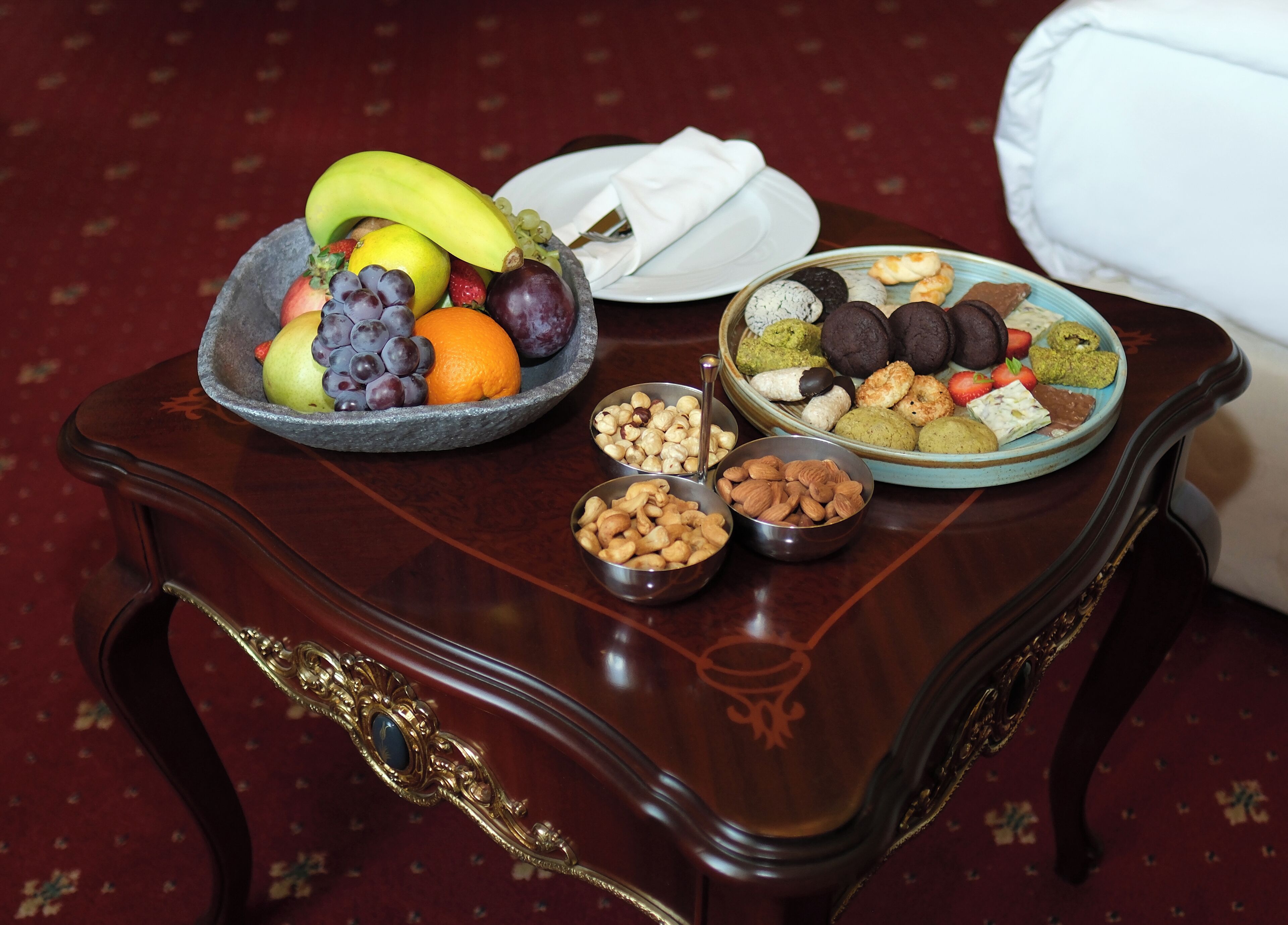 Uma mesa de madeira com uma cesta de frutas, um prato de biscoitos e recipientes com nozes.