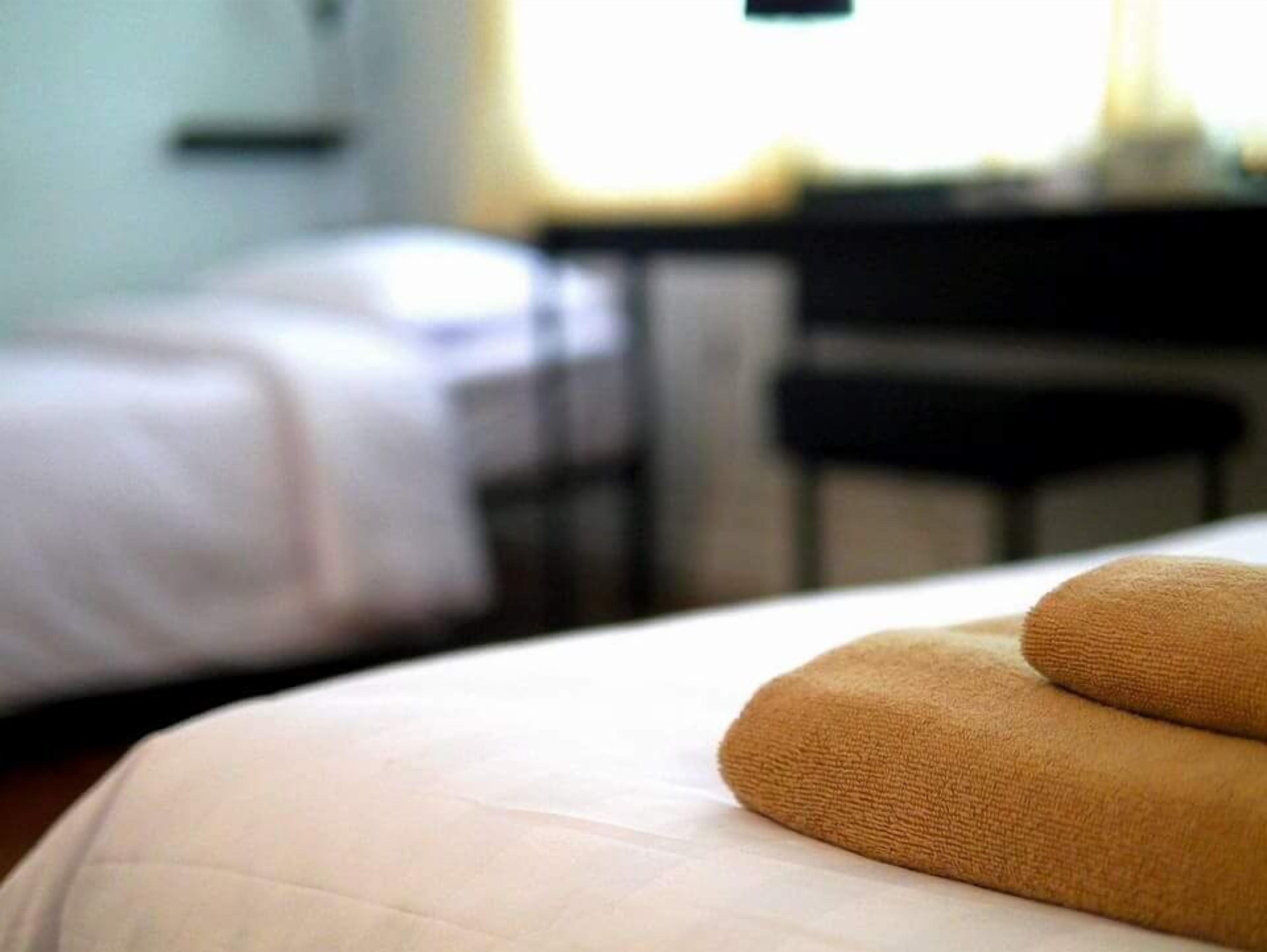 Cama com lençol branco e travesseiro marrom em quarto de hotel.