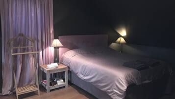 Quarto com cama, luminárias de cabeceira, mesa de cabeceira de madeira e um cabideiro.