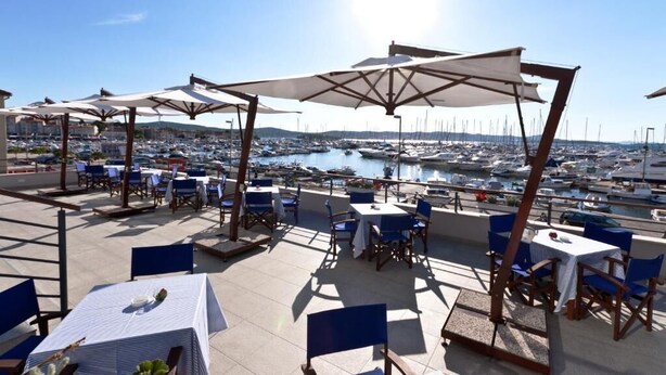 Terraço com mesas e cadeiras, com vista para uma marina com barcos.