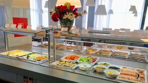 Buffet com diversas opções de comida, um vaso de flores e uma placa vermelha à esquerda.