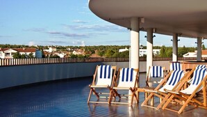 Área de piscina no terraço com espreguiçadeiras e vista para uma área residencial.