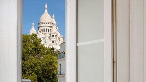 Uma janela com vista para um edifício branco com cúpulas, uma árvore e uma rua.