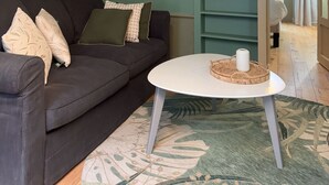 Sala de estar com um sofá escuro, uma mesa de centro branca, luminária pendente de fibra natural e parede verde.