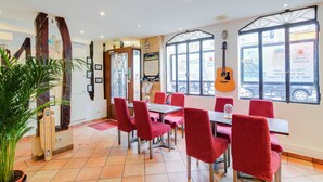 Restaurante com cadeiras vermelhas, uma guitarra de madeira e uma grande janela com vista para a rua.