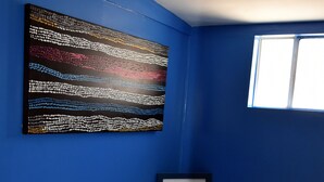 Quarto com paredes azuis, uma grande obra de arte abstrata, um quadro emoldurado e um banco branco.