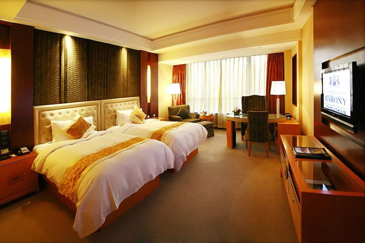Quarto de hotel com duas camas, uma escrivaninha, uma cadeira, televisão e minibar.