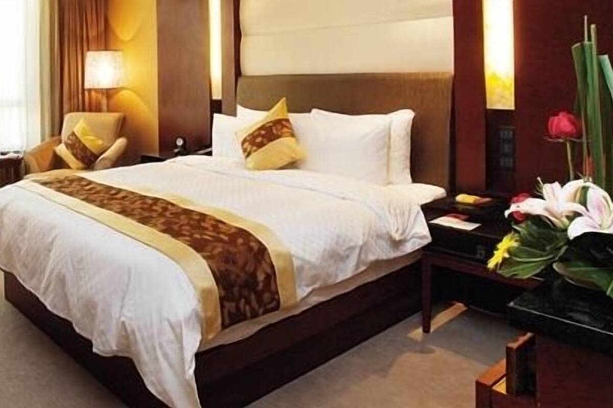 Quarto de hotel com uma cama grande, uma escrivaninha, uma cadeira e uma mesa de cabeceira com um vaso de flores.