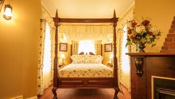 Uma cama com dossel adornada com roupa de cama florida, uma lareira e um vaso de flores sobre a lareira.