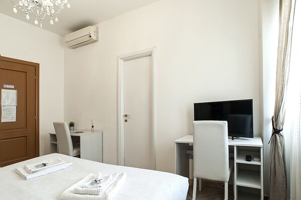 Quarto de hotel com cama, escrivaninha, cadeira, televisão e ar condicionado.