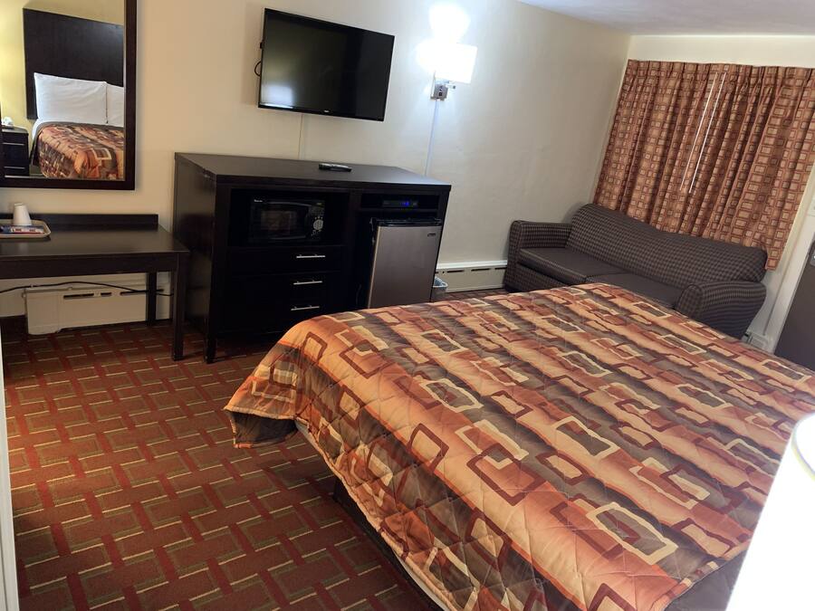 Quarto de hotel com cama, escrivaninha, televisão, micro-ondas e frigorífico.
