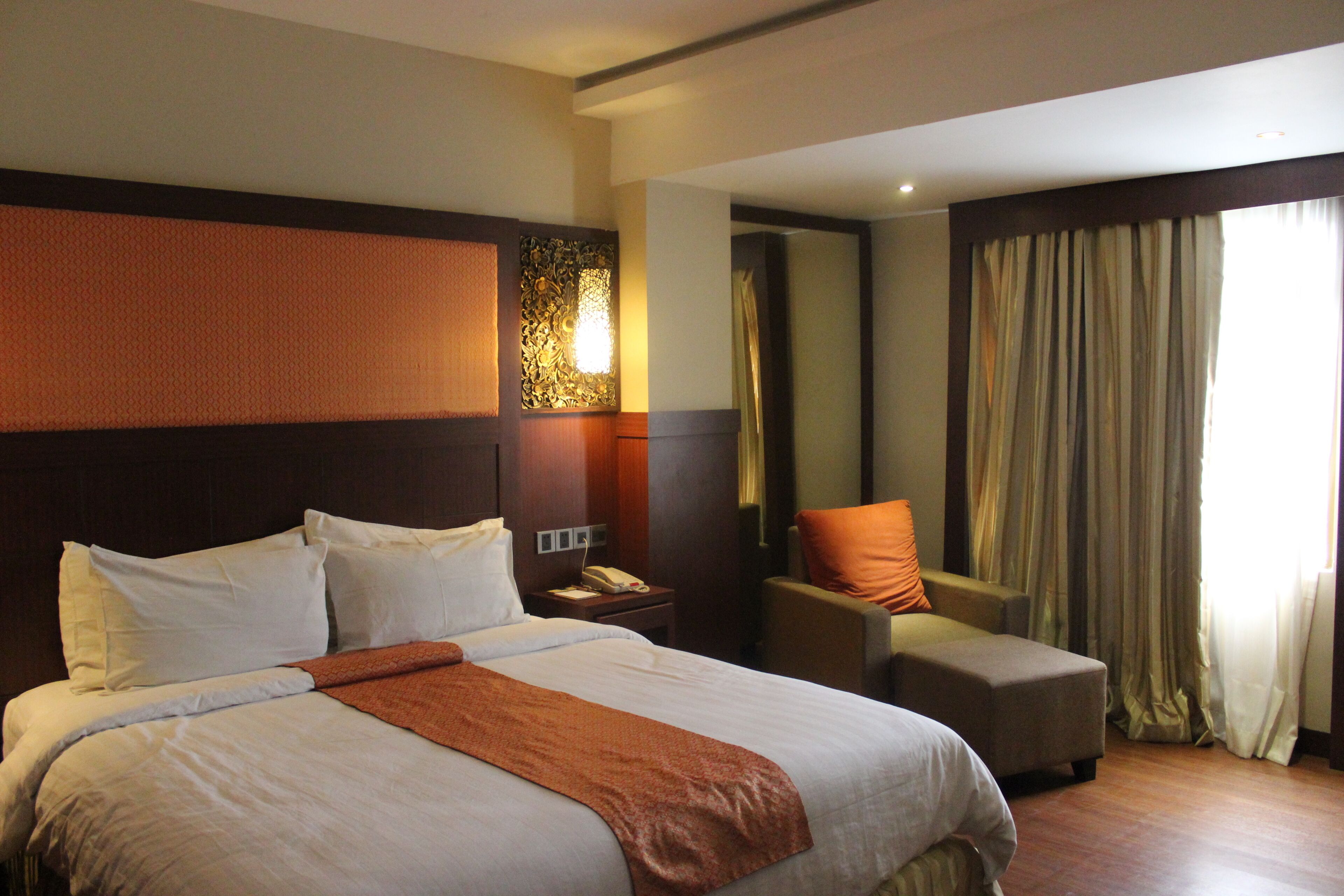 Quarto de hotel com uma cama grande, uma escrivaninha com telefone, uma cadeira e uma janela com cortinas.