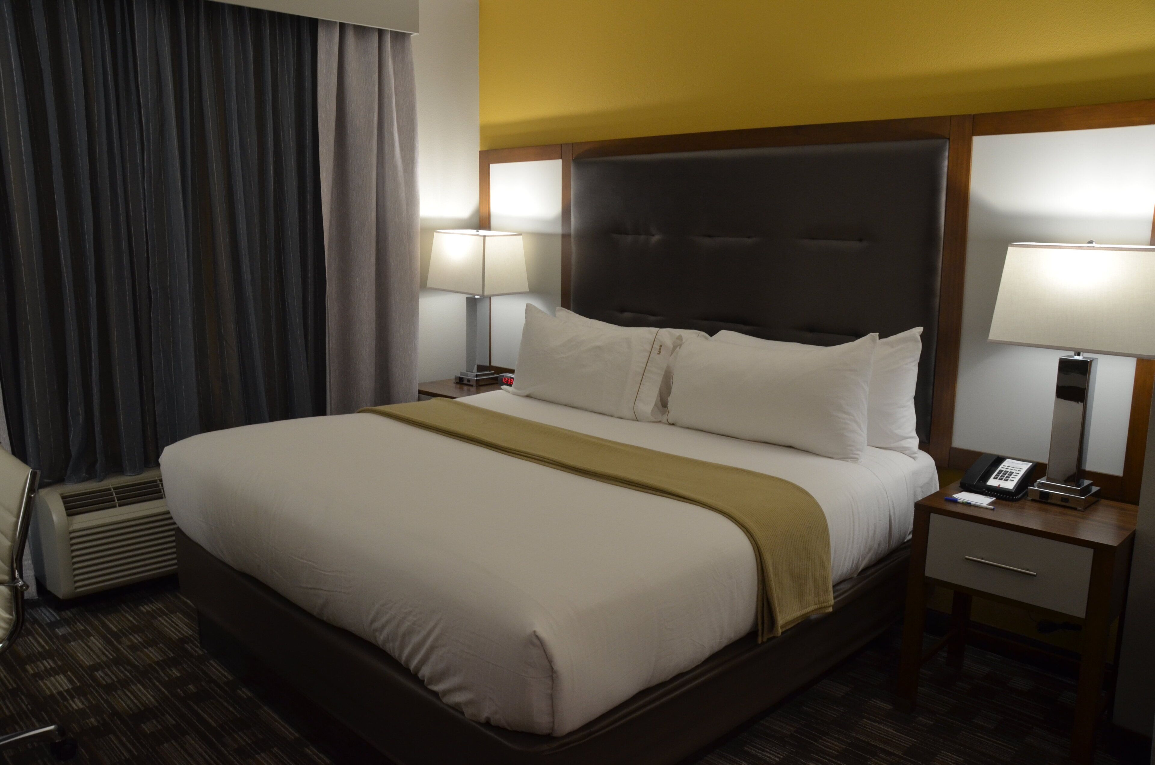 Quarto de hotel com uma cama grande, abajures, mesa de cabeceira com telefone e janela com cortinas.
