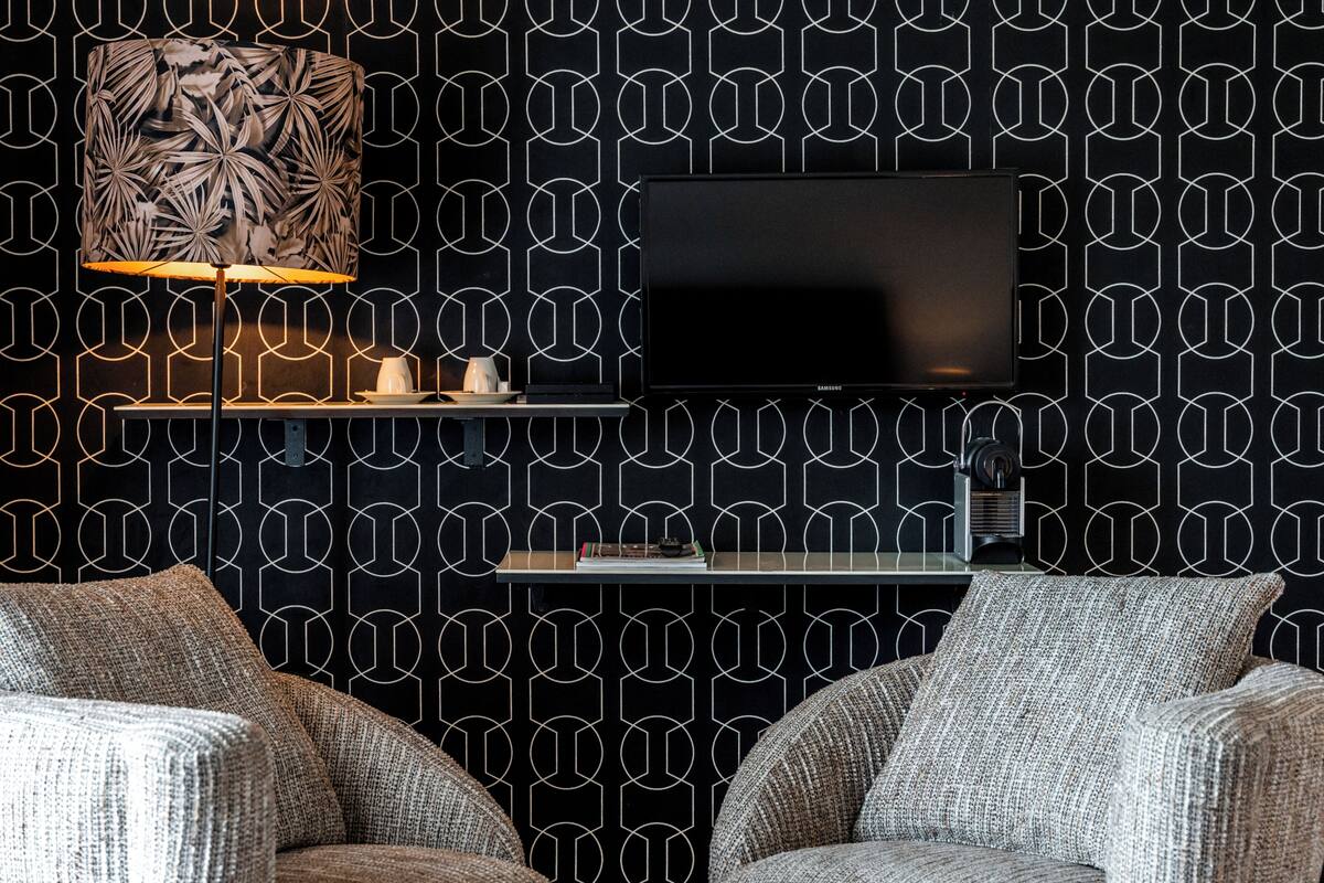 Uma sala de estar moderna com papel de parede estampado, uma TV de tela plana na parede, um abajur e dois sofás.