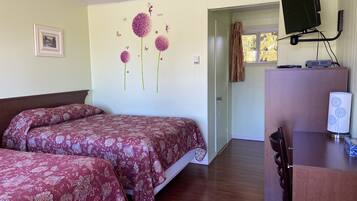 Quarto de hotel com duas camas, uma escrivaninha, televisão e uma parede com decoração floral.