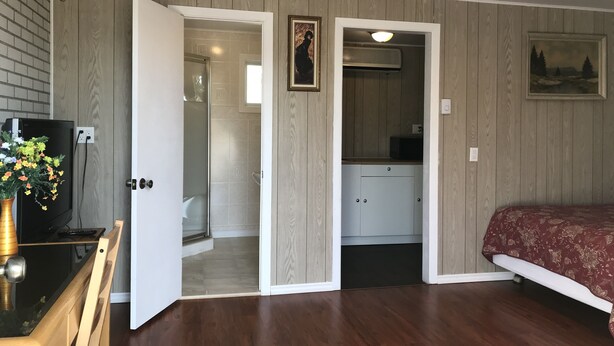 Quarto com piso de madeira, cama com colcha florida, televisão em um suporte e porta que dá para um banheiro.
