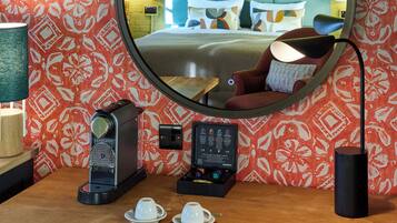 Quarto de hotel com um espelho redondo refletindo uma cama, uma máquina de café e duas chávenas na mesa.
