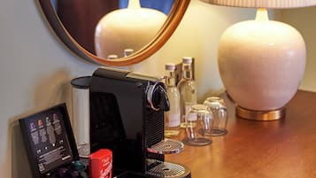 Cantinho com café, incluindo cafeteira, xícaras e um espelho refletindo uma luminária e uma cadeira vermelha.