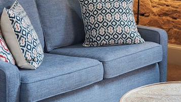 Uma sala de estar moderna com um sofá azul, almofadas estampadas, um objeto esférico vermelho e um abajur.