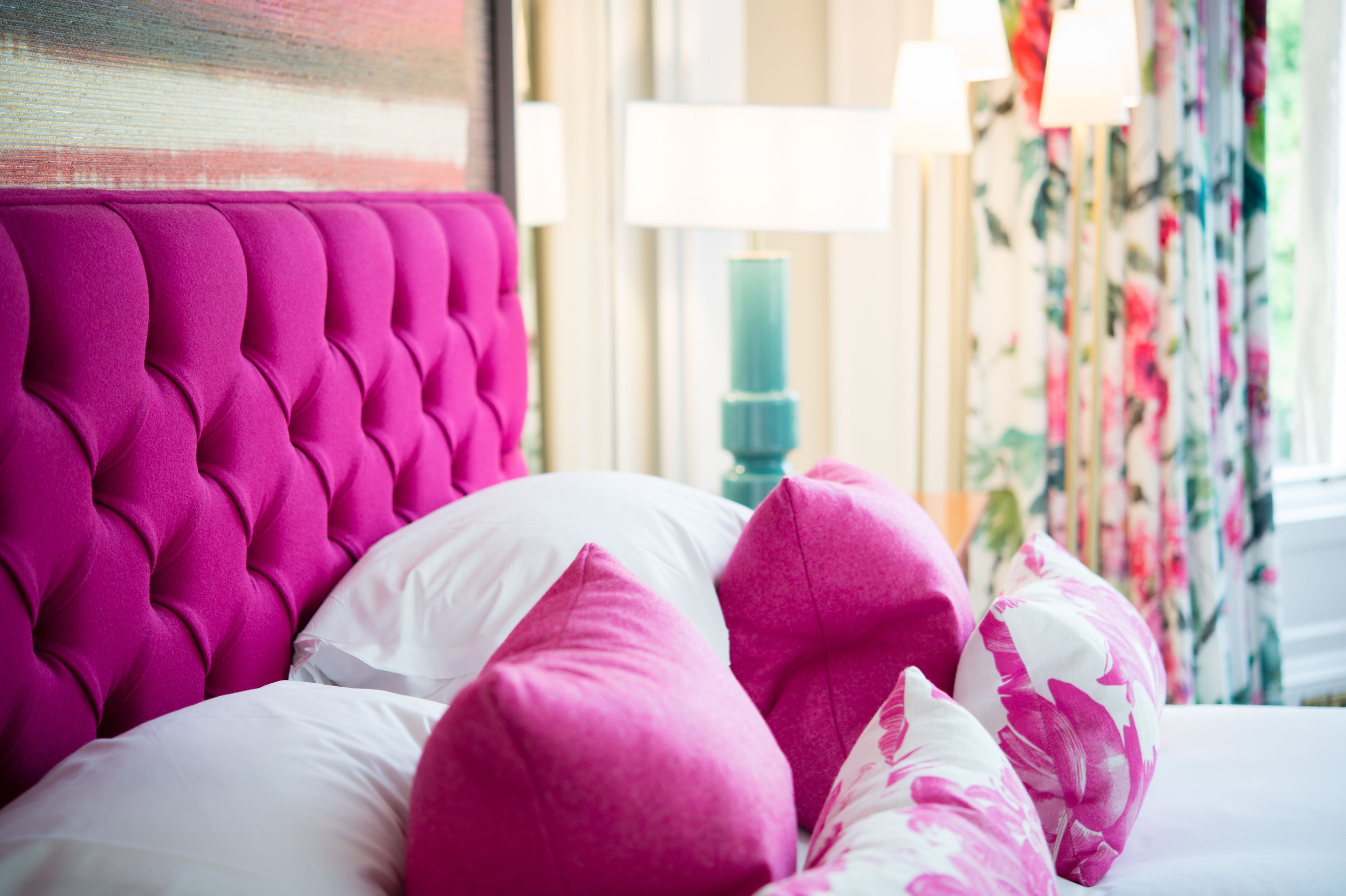 Cama com cabeceira estofada e várias almofadas em tons de rosa e branco.