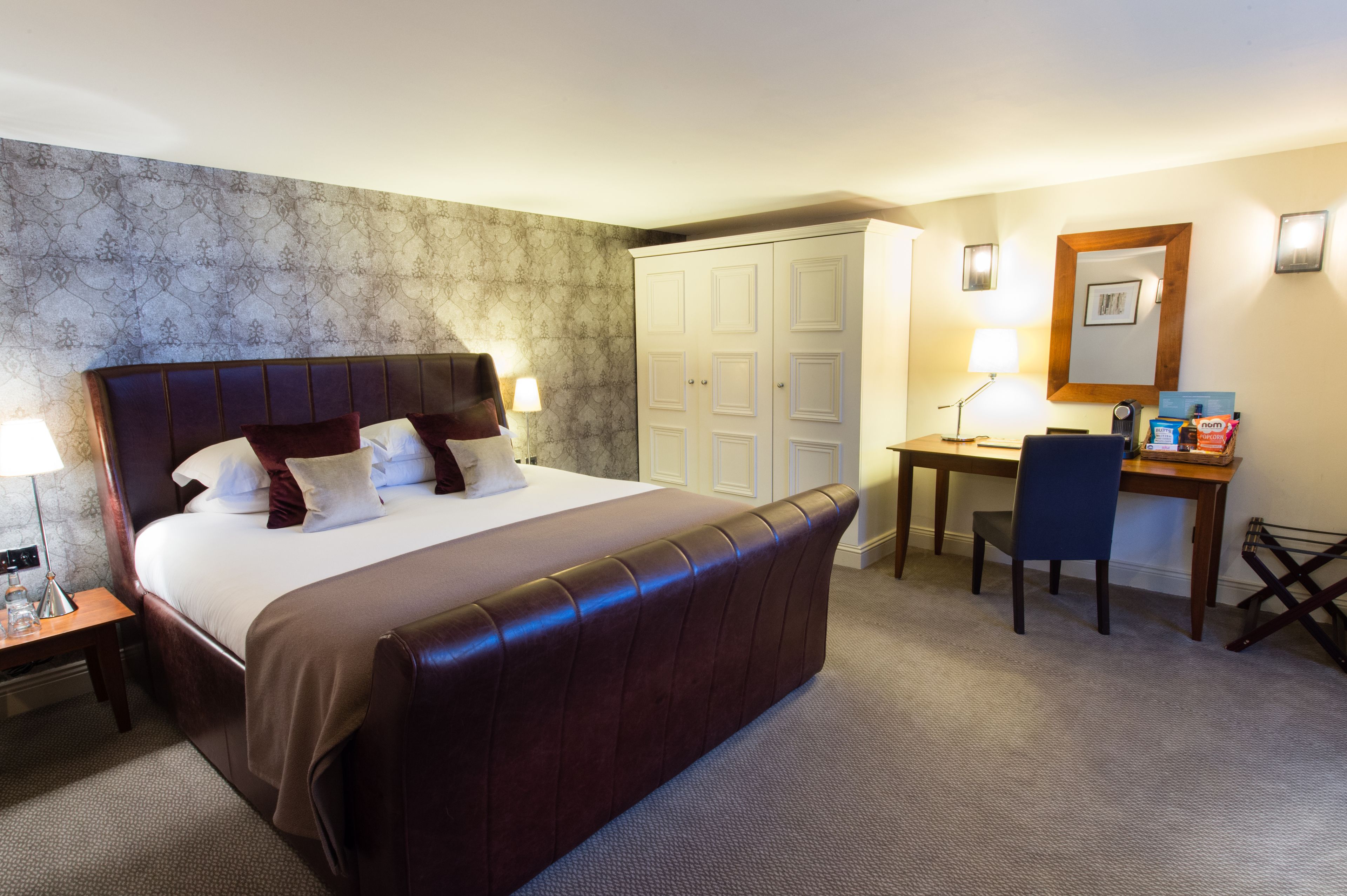 Quarto de hotel com cama grande, escrivaninha, cadeira, guarda-roupa e espelho.