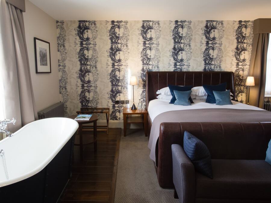 Quarto de hotel com cama grande, área de estar com sofá, banheira e papel de parede estampado.