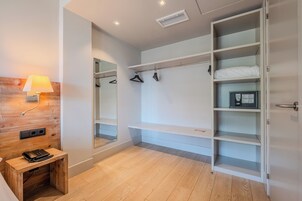 Um closet espaçoso com portas abertas, um espelho, uma barra para pendurar roupas e um criado-mudo de madeira com um telefone.