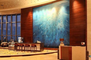 Um lobby com um grande mural abstrato, uma receção, área de bar e assentos.