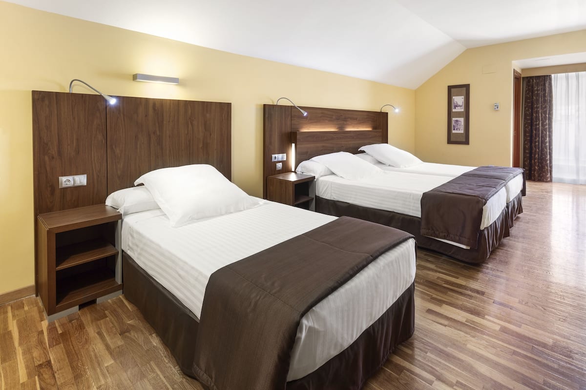 Quarto de hotel com duas camas, cabeceiras de madeira, mesas de cabeceira e uma janela grande com cortinas.