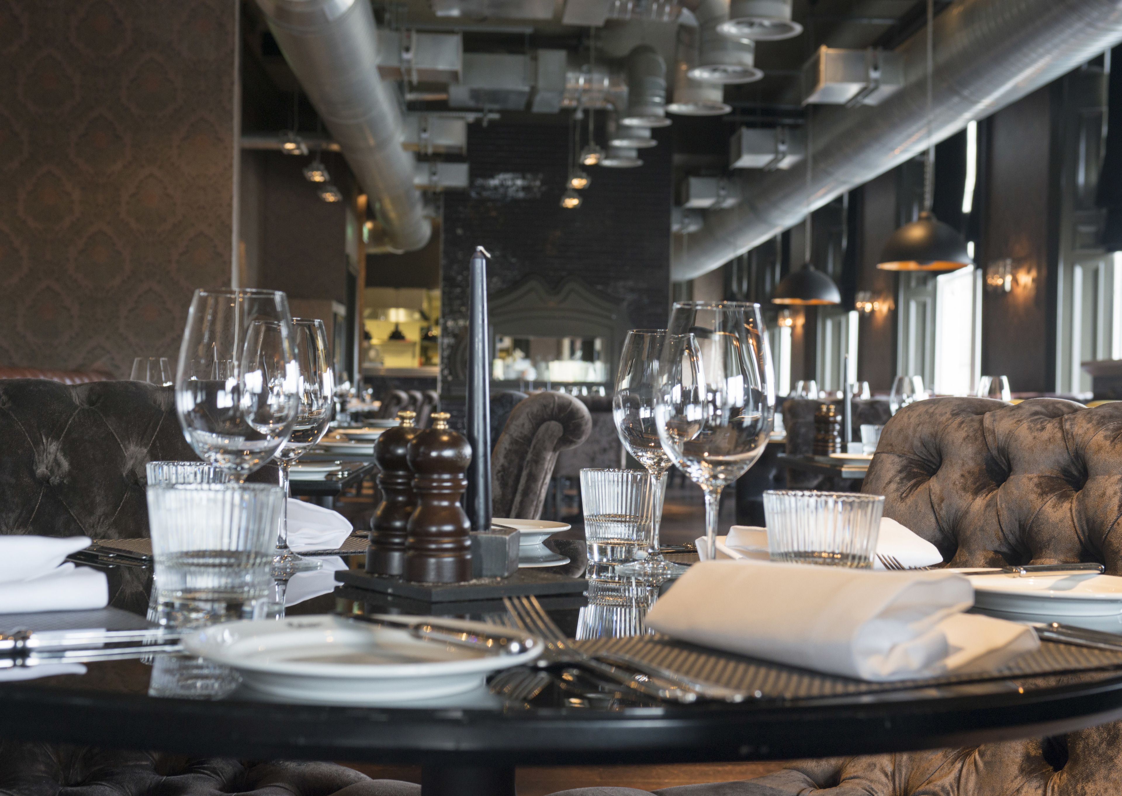 Interior de restaurante com uma longa mesa de jantar posta para uma refeição, com vários copos de vinho, pratos e talheres.