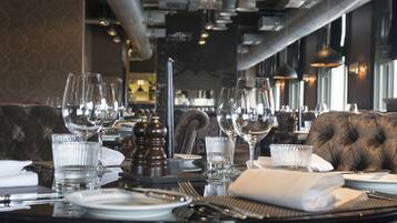 Interior de restaurante com uma longa mesa de jantar posta para uma refeição, com vários copos de vinho, pratos e talheres.