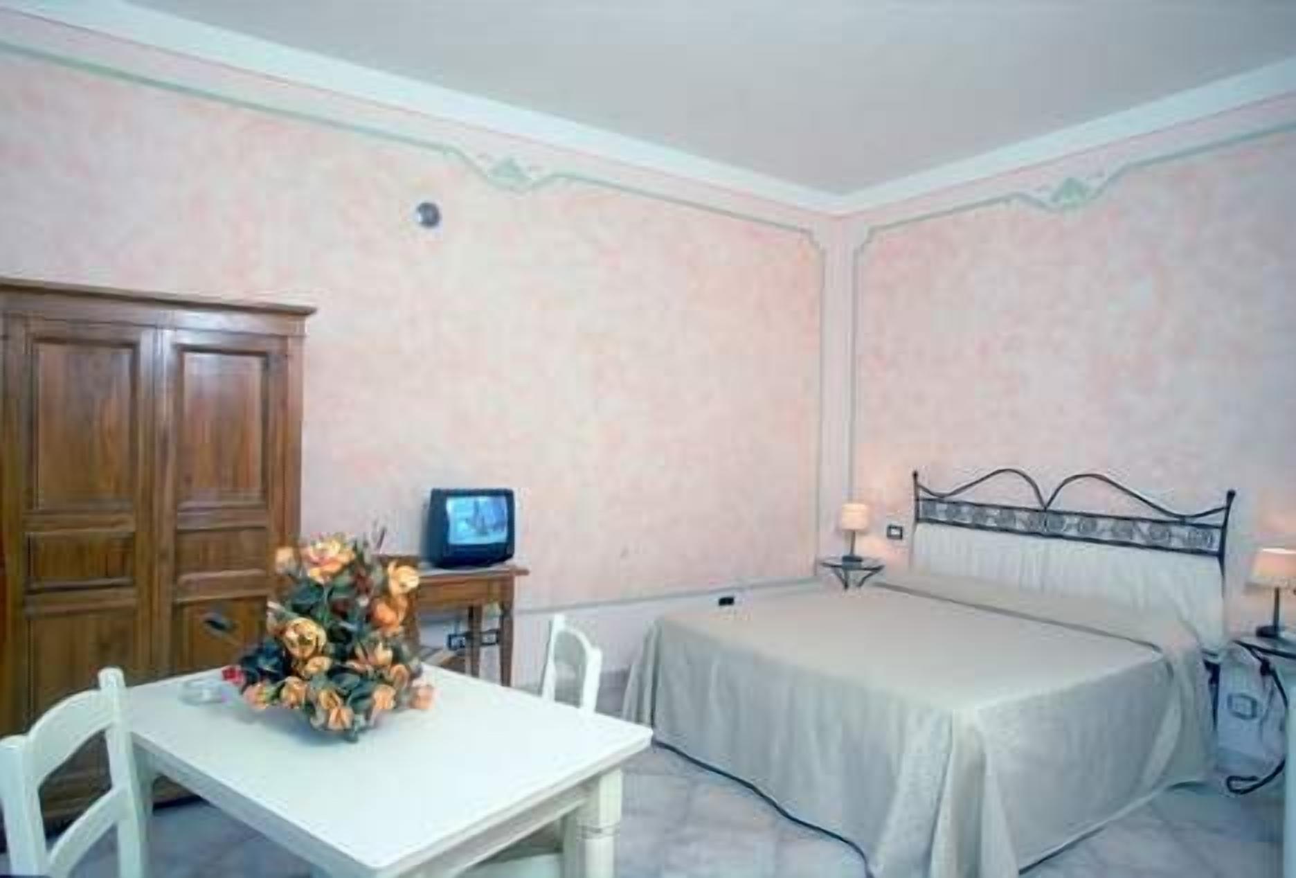 Quarto com cama, televisão sobre uma mesinha, escrivaninha com um vaso de flores e guarda-roupa.