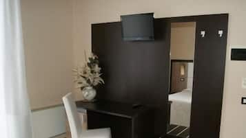 Quarto de hotel com cama, mesa de trabalho, televisão de tela plana, cadeira e vaso com flores.