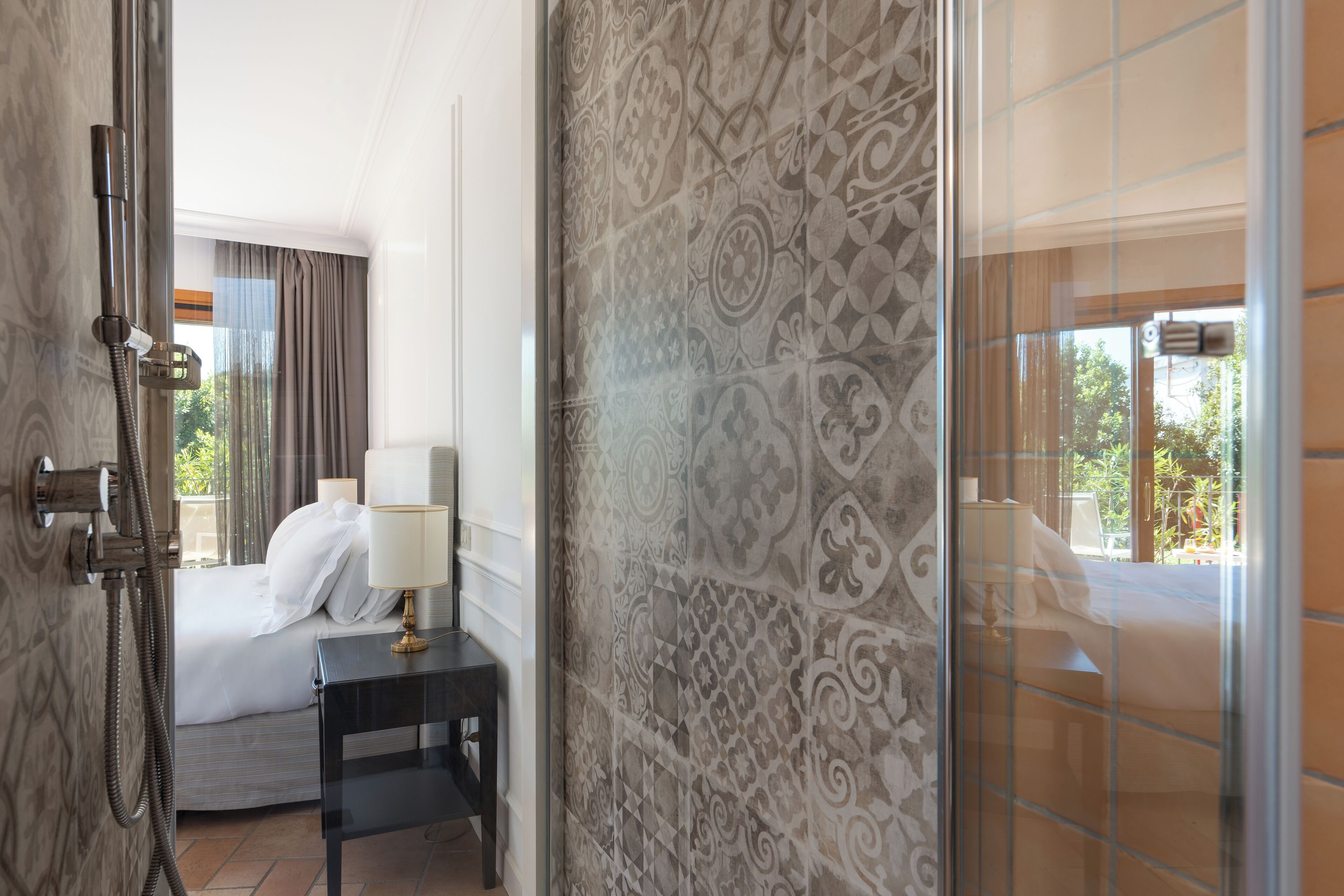 Quarto de hotel com cama, mesa de cabeceira com abajur, área de chuveiro e paredes com padrão.