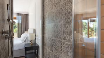 Quarto de hotel com cama, mesa de cabeceira com abajur, área de chuveiro e paredes com padrão.