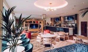 Um hall de hotel moderno com área de bar, opções de assento e uma tela de televisão.