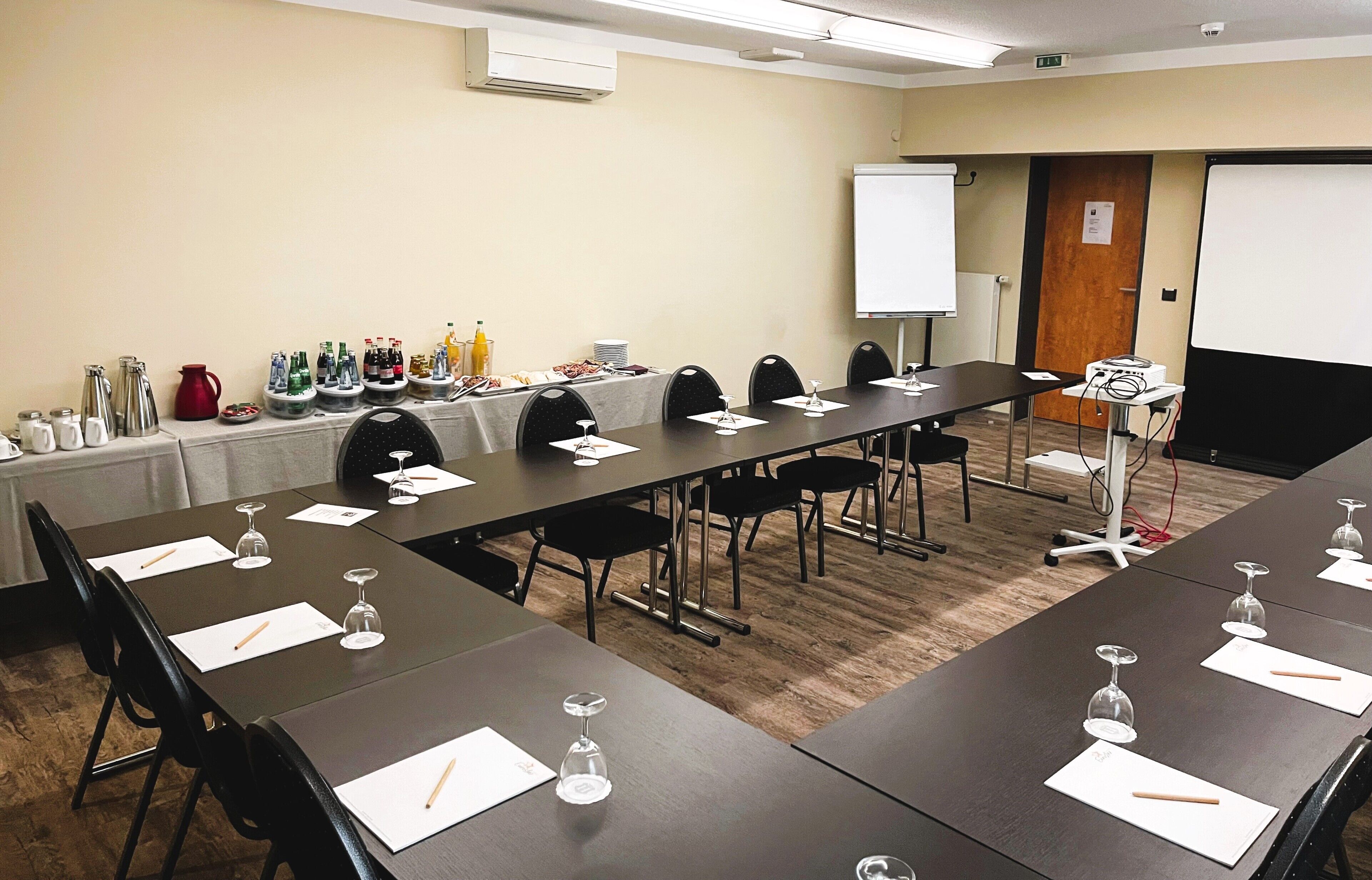Uma sala de conferências com mesas longas, cadeiras, um quadro branco e um projetor.