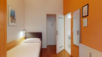 Quarto de hotel com uma cama, mesa de cabeceira, luminária fixada na parede e um quadro emoldurado. Há uma porta que dá para um banheiro.