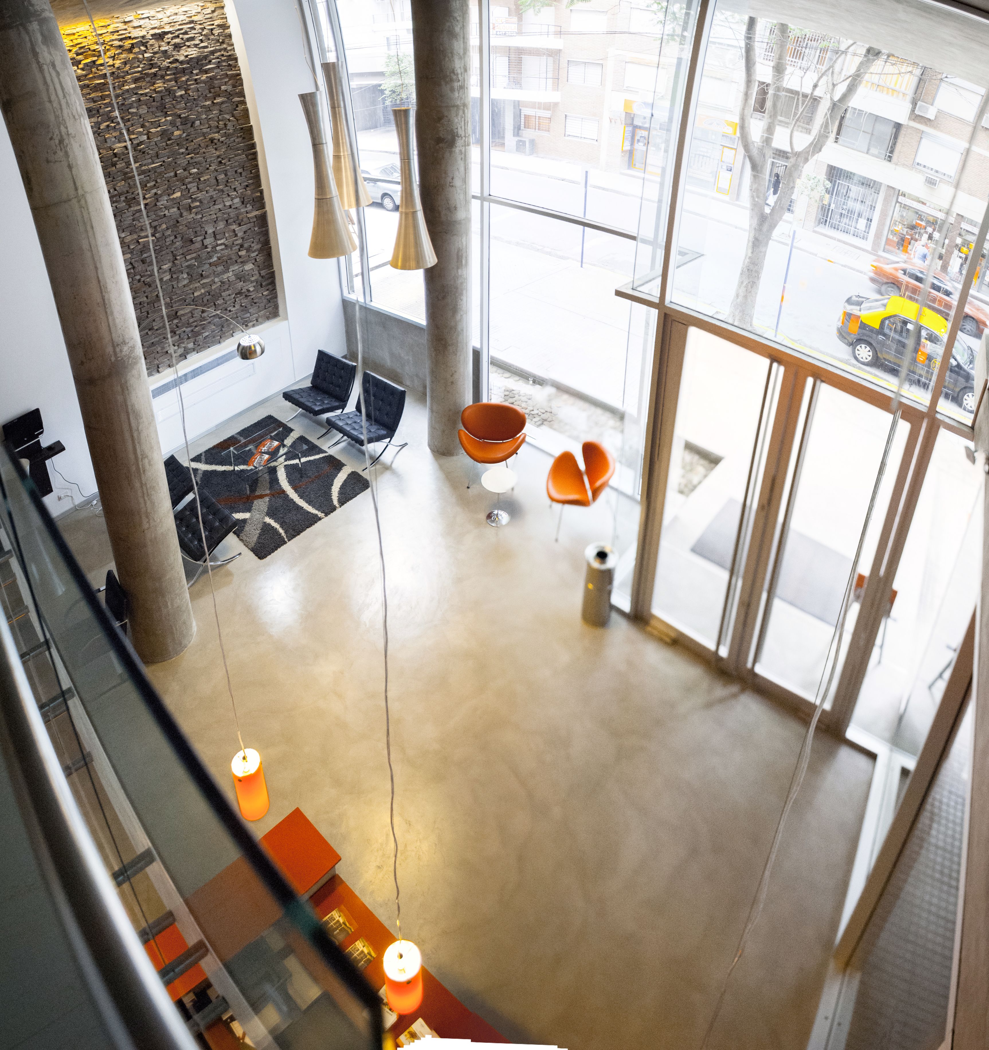 Um hall amplo com design moderno, apresentando uma parede de pedra, assentos contemporâneos e grandes janelas com vista para a rua.