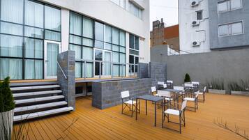 Um pátio externo com área de bar, assentos e escada que leva a um andar superior.