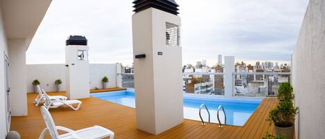 Área de piscina no terraço, com espreguiçadeiras, piscina e vista para a cidade.