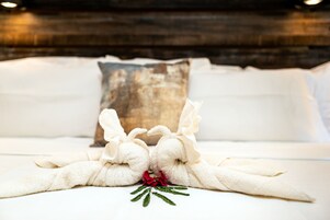 Cama bem arrumada com lençóis brancos e uma composição decorativa de toalhas em formato de coelhos.