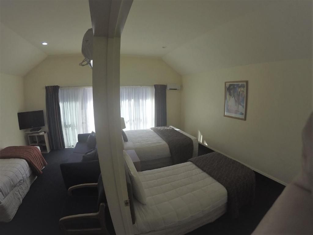 Quarto de hotel com cama, escrivaninha, cadeira e televisão.