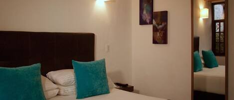 Quarto com uma cama grande, duas almofadas azul-turquesa, uma cabeceira escura e duas luminárias fixadas na parede.