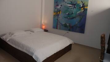 Quarto com cama, mesa de cabeceira, luminária, cadeira e uma grande pintura abstrata na parede.