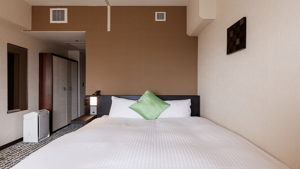 Quarto de hotel com cama, radiador, guarda-roupa e porta que dá para outro cômodo.
