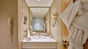 Casa de banho de hotel com lavatório, espelho, secador de cabelo e suporte para roupões.