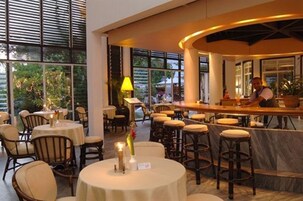 Um restaurante com mesas redondas, banquetas de bar e um espaço de bar.